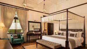 Uma cama com dossel e cortina, uma poltrona verde, uma escrivaninha de madeira e uma janela grande com cortinas.