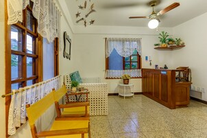Uma cozinha acolhedora com móveis de madeira, um ventilador de teto e detalhes decorativos como cortinas de renda e quadros nas paredes.