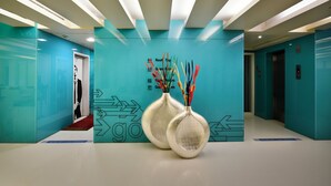 Um lobby moderno com paredes verde-água, divisória de vidro e dois vasos com gravetos coloridos.