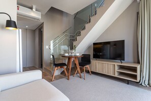 Uma sala de estar moderna com sofá, mesa de jantar com cadeiras, televisão de tela plana e escada.