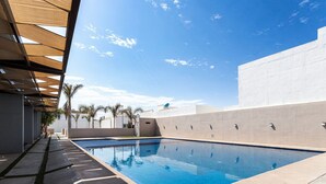 Piscina com superfície de água azul límpida, rodeada por um deck de concreto e uma estrutura de pérgula.