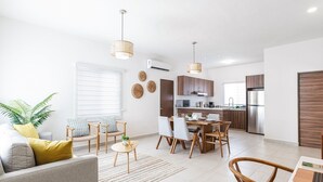 Uma sala de estar moderna com sofá, mesa de jantar e cadeiras, cozinha com armários de madeira e uma janela grande.