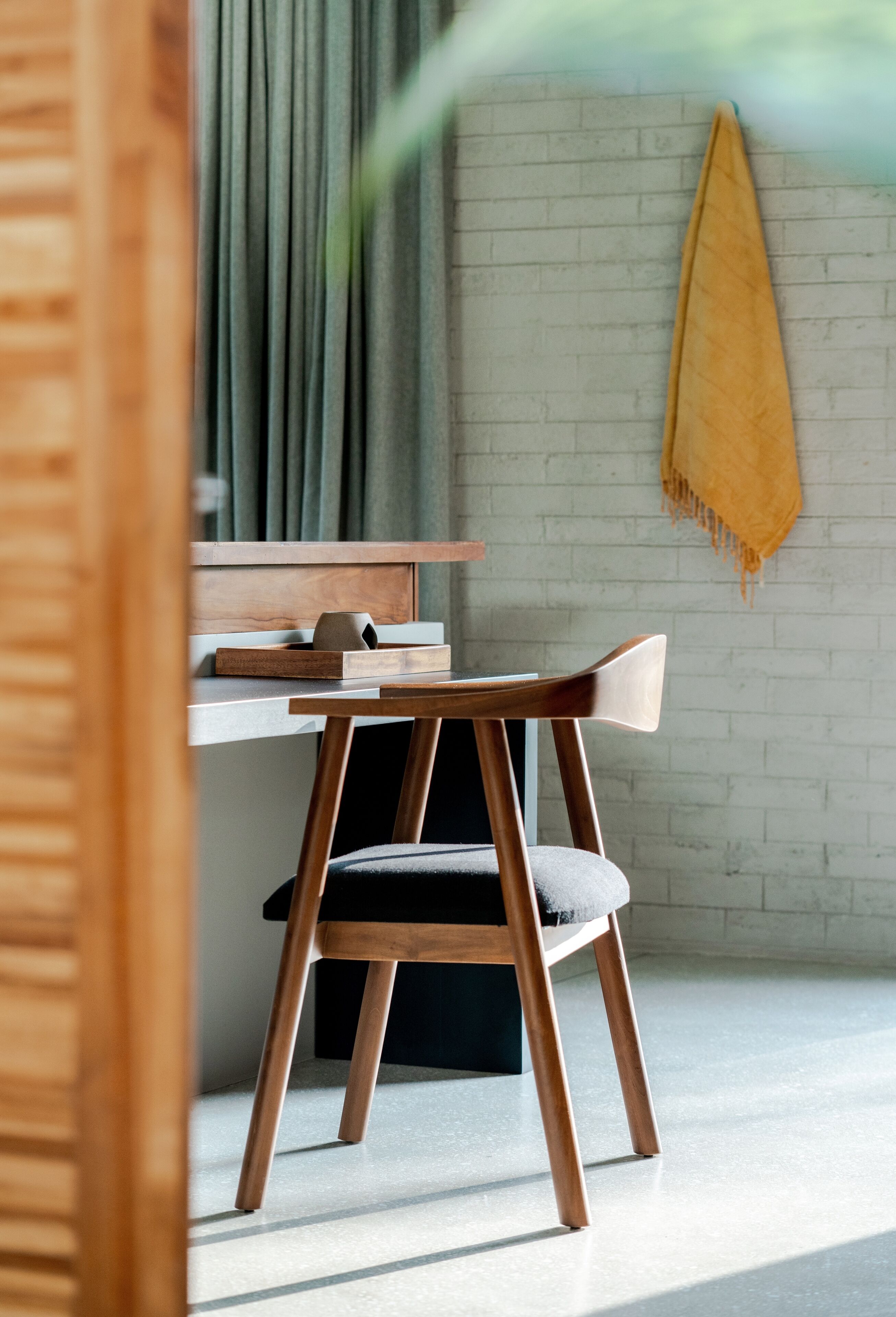 Uma área de refeições moderna com mesa e cadeiras de madeira, parede de tijolos cinzentos e um cobertor amarelo pendurado na parede.
