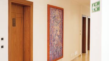 Um corredor com portas de madeira, um quadro abstrato emoldurado e um sinal de saída de emergência verde.