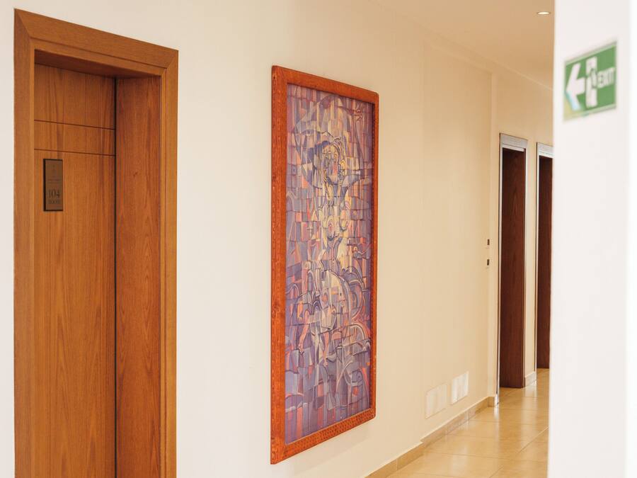 Um corredor com portas de madeira, um quadro abstrato emoldurado e um sinal de saída de emergência verde.