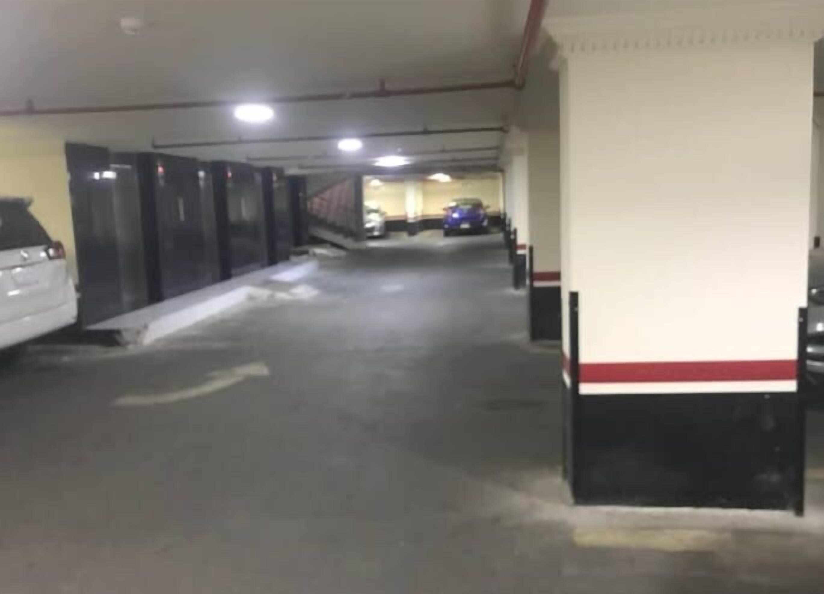 Um estacionamento com vários níveis, pisos de concreto e estrutura de colunas brancas e vermelhas.