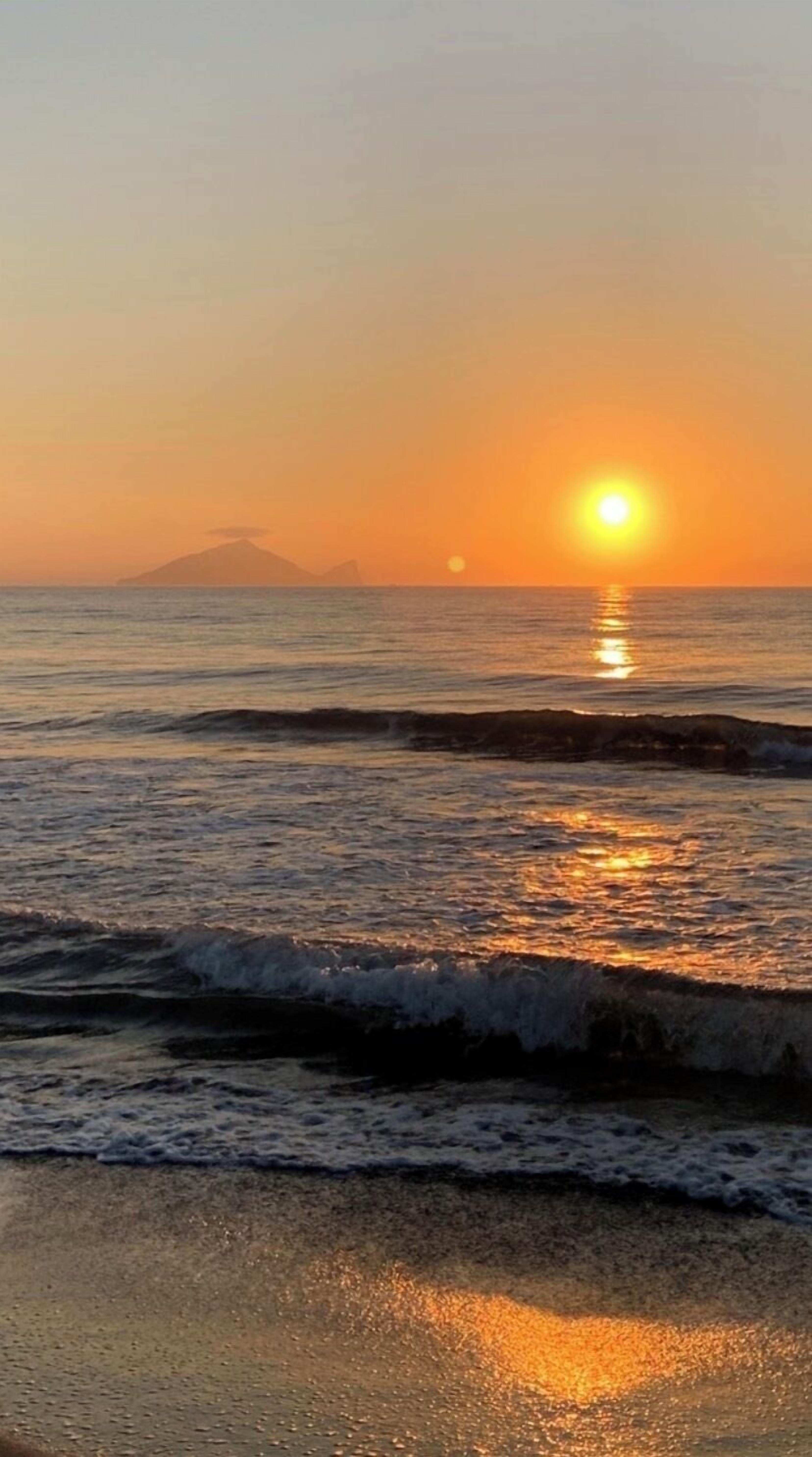 Um pôr do sol sobre uma praia com ondas.