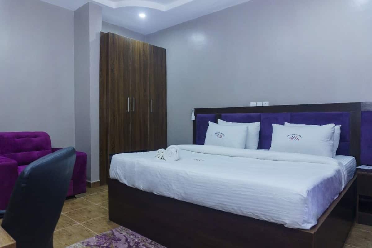 Um quarto com uma cama, uma cadeira roxa e um guarda-roupa.