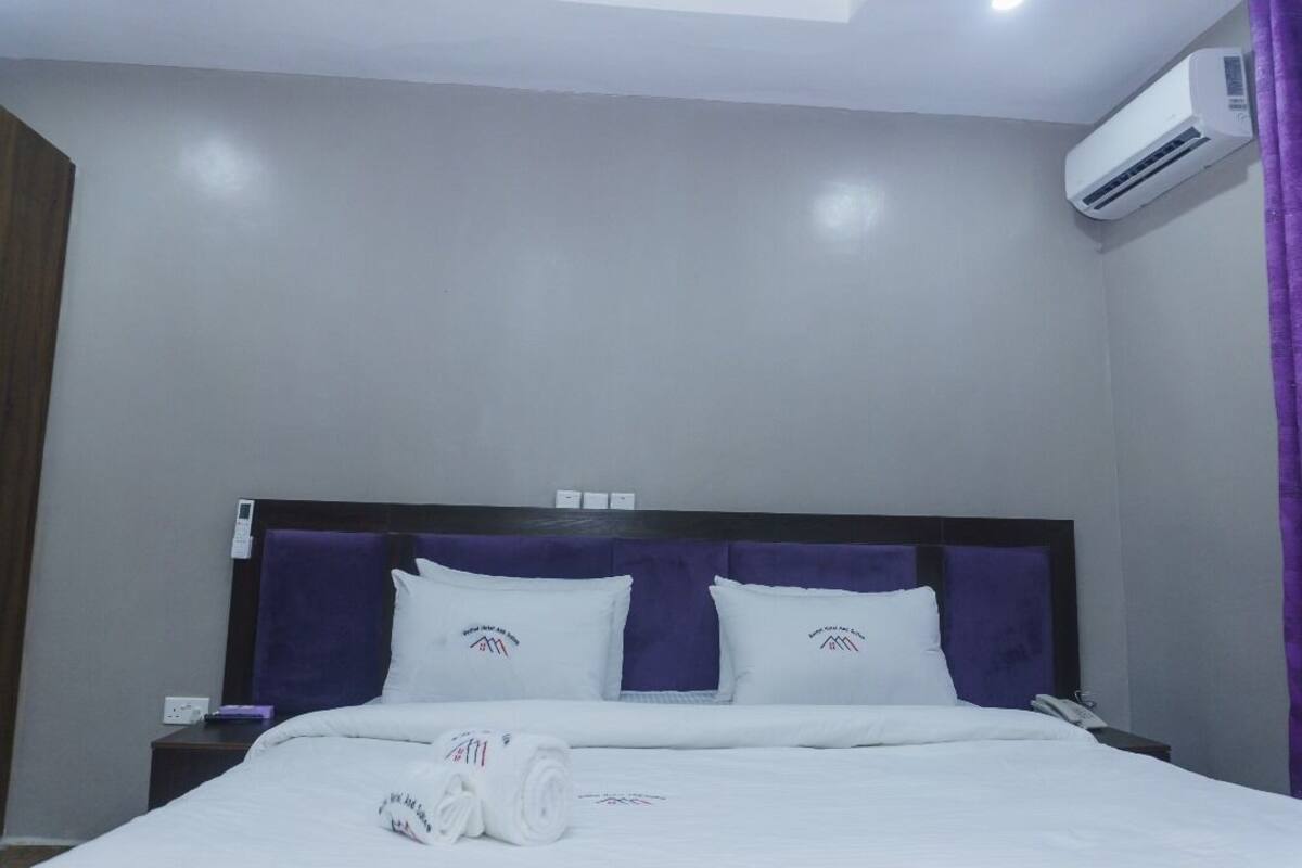 Quarto de hotel com cama bem arrumada, mesa de cabeceira e ar condicionado na parede.