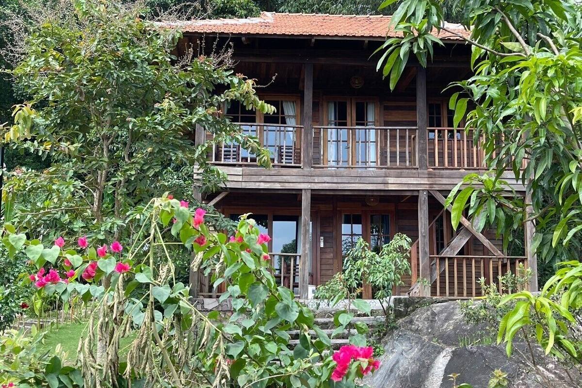 Uma casa de madeira com varanda, rodeada por vegetação exuberante e plantas floridas.