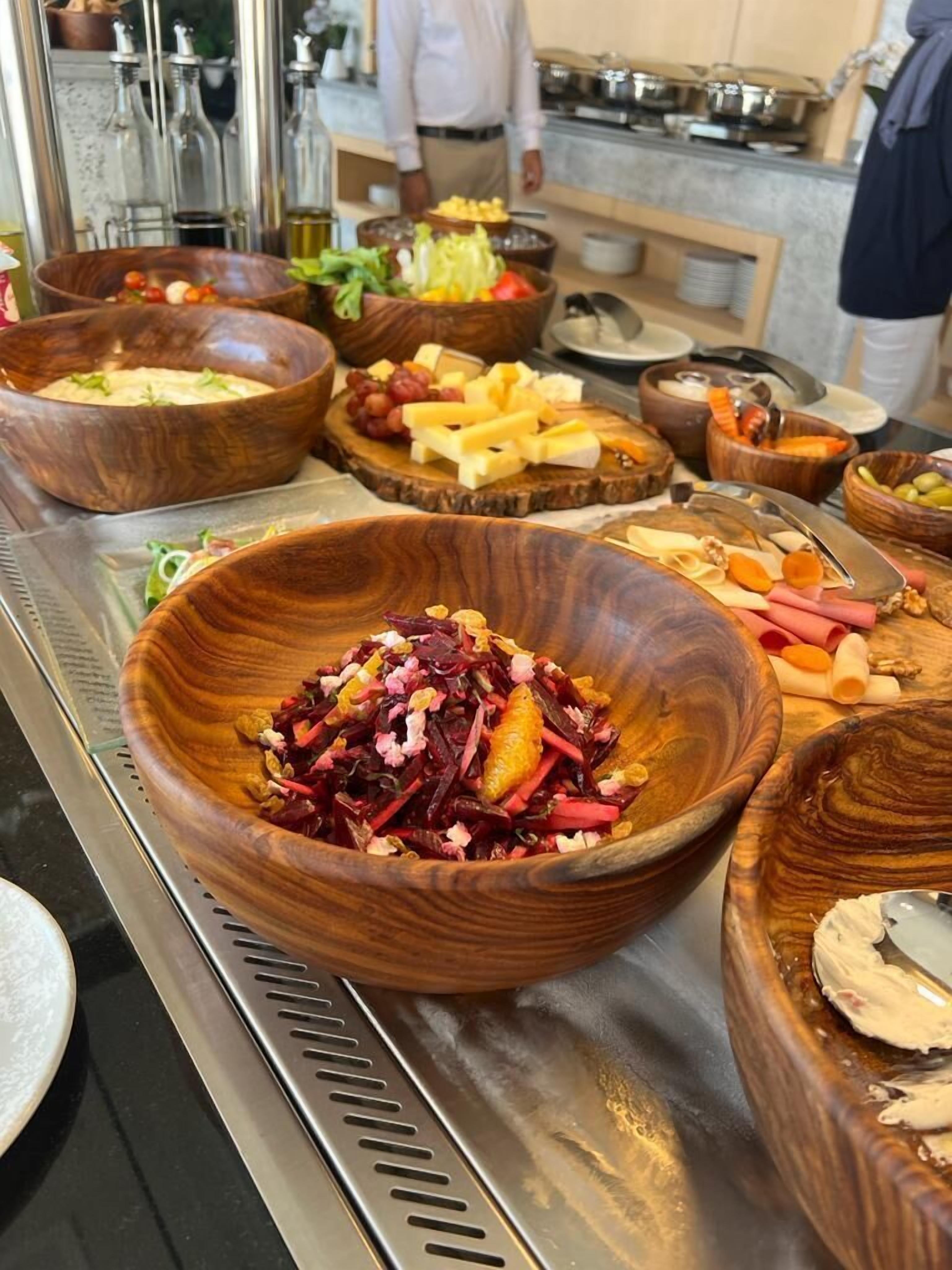 Buffet com diversos alimentos em tigelas de madeira, incluindo frutas, vegetais e queijos.