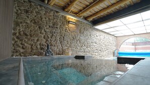 Piscina interior com paredes de pedra e teto de madeira.