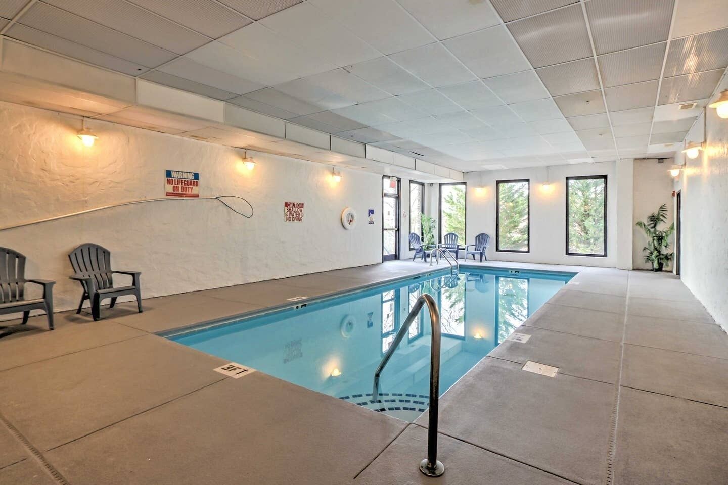 Piscina interior com superfície de água cristalina, cercada por paredes com placas de segurança e uma área de estar com cadeiras.