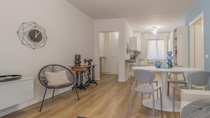 Uma sala de estar moderna com área de jantar, um relógio de arame preto, uma mesa de madeira e um sofá.