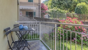 Varanda com mesa e cadeiras, corrimão e vista para um jardim com flores cor-de-rosa.