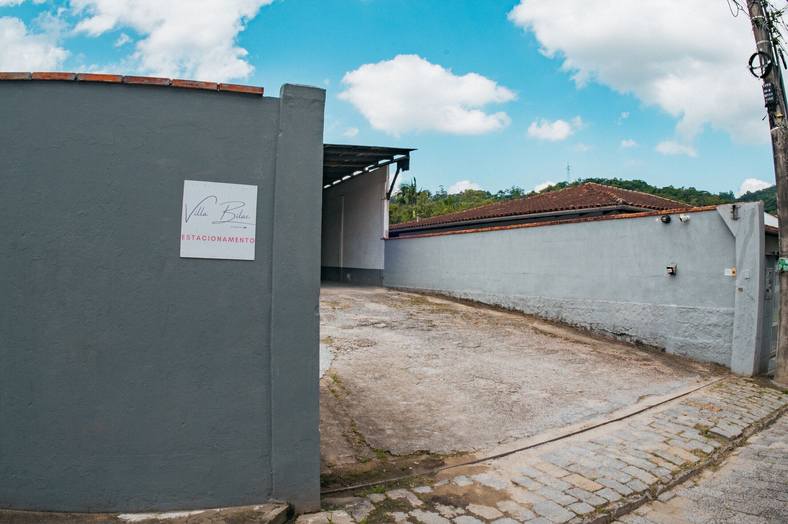 Um edifício cinzento com uma placa que diz 'Villa Buey Estacionamento' e uma área pavimentada que leva a uma entrada coberta.