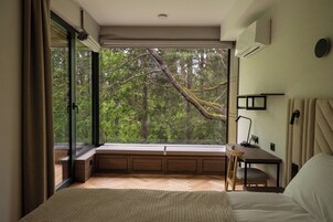 Quarto com uma janela grande, cama, escrivaninha e cadeira.