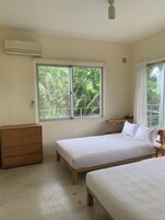 Quarto com duas camas, cômoda de madeira e janela com vista para o verde.