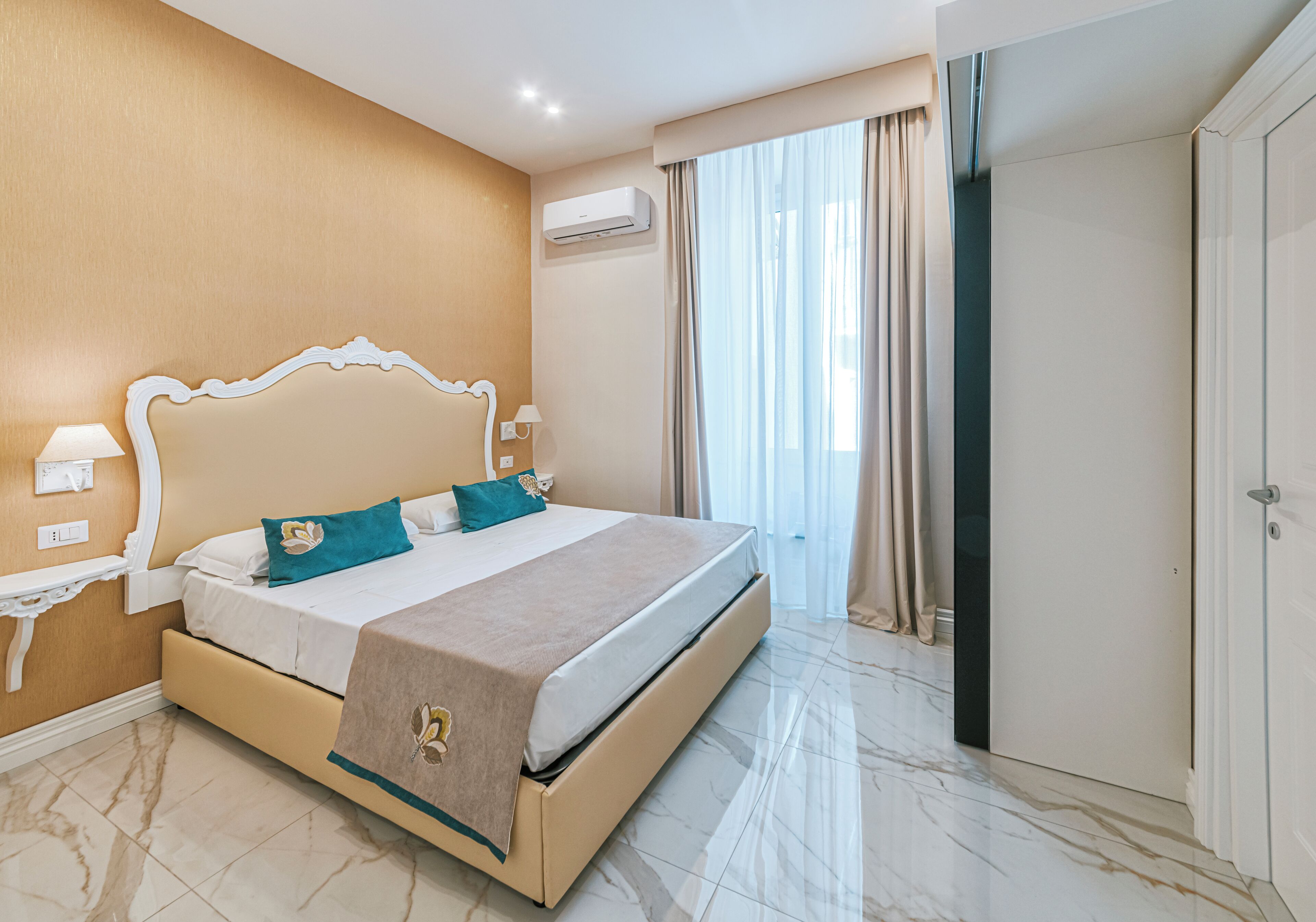 Quarto de hotel com uma cama grande, um guarda-roupa, ar condicionado e uma janela com cortinas.