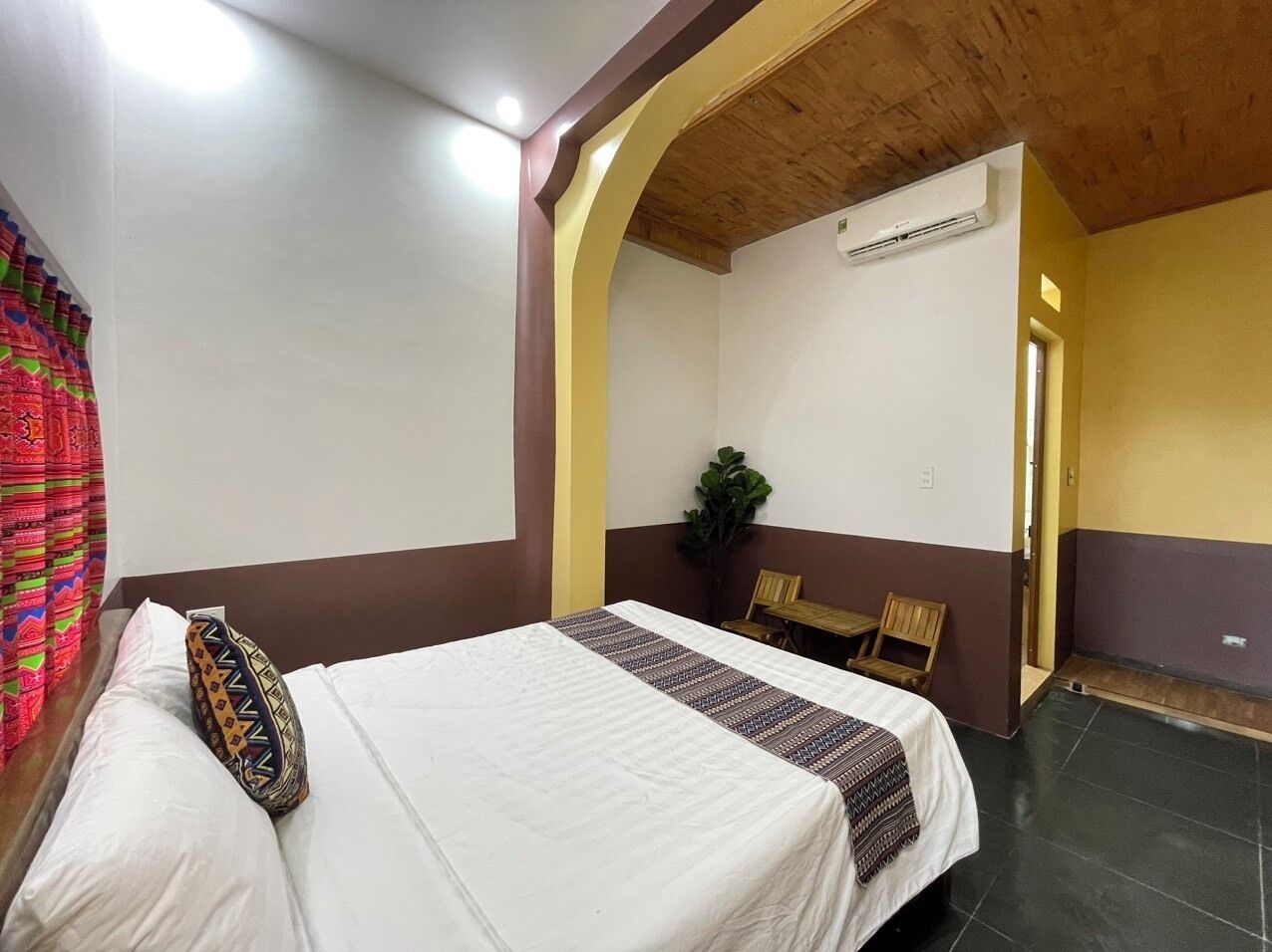 Quarto de hotel com cama, uma cadeira, uma mesinha e um vaso de planta.