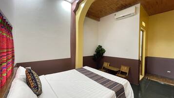 Quarto de hotel com cama, uma cadeira, uma mesinha e um vaso de planta.