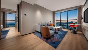 Quarto de hotel moderno com sofá, poltronas, uma mesinha de centro e vista da cidade através de amplas janelas.