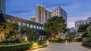 Uma área residencial urbana moderna, com edifícios altos, áreas verdes bem cuidadas e caminhos iluminados.