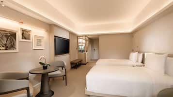 Quarto de hotel com uma cama grande, televisão, mesa pequena com cadeira e um banquinho.