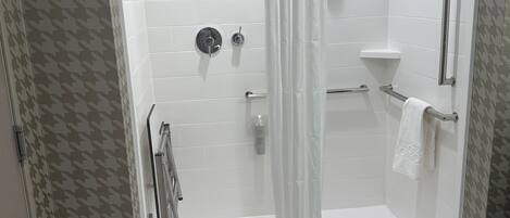 Uma área de chuveiro moderna com porta de vidro, chuveiro manual, porta-toalhas e vaso sanitário.