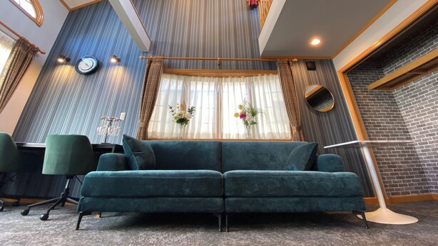 Uma sala de estar moderna com um sofá azul-turquesa, uma mesa redonda e uma grande janela com cortinas.