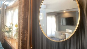 Quarto com um espelho grande refletindo um interior moderno, uma TV de tela plana fixada na parede e um espaço de jantar com mesa e cadeiras.