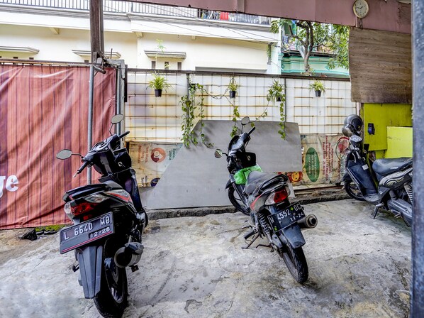 Uma motocicleta estacionada em área coberta, com piso de concreto, uma faixa vermelha e parede com plantas penduradas.