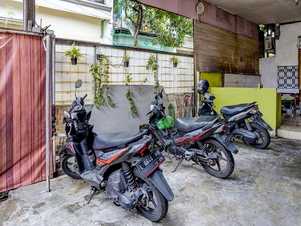 Duas motocicletas estacionadas em área coberta com piso de concreto, parede de madeira e porta verde.