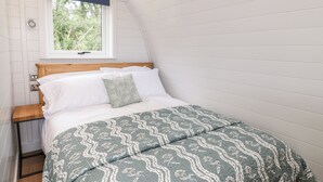 Quarto com cama, janela e vista para o verde lá fora.