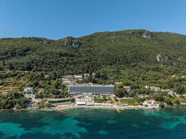 Um hotel à beira-mar com um edifício moderno, comodidades na praia e vegetação exuberante.
