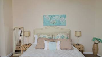 Quarto com cama, duas mesas de cabeceira, um espelho, um quadro e um vaso com flores.