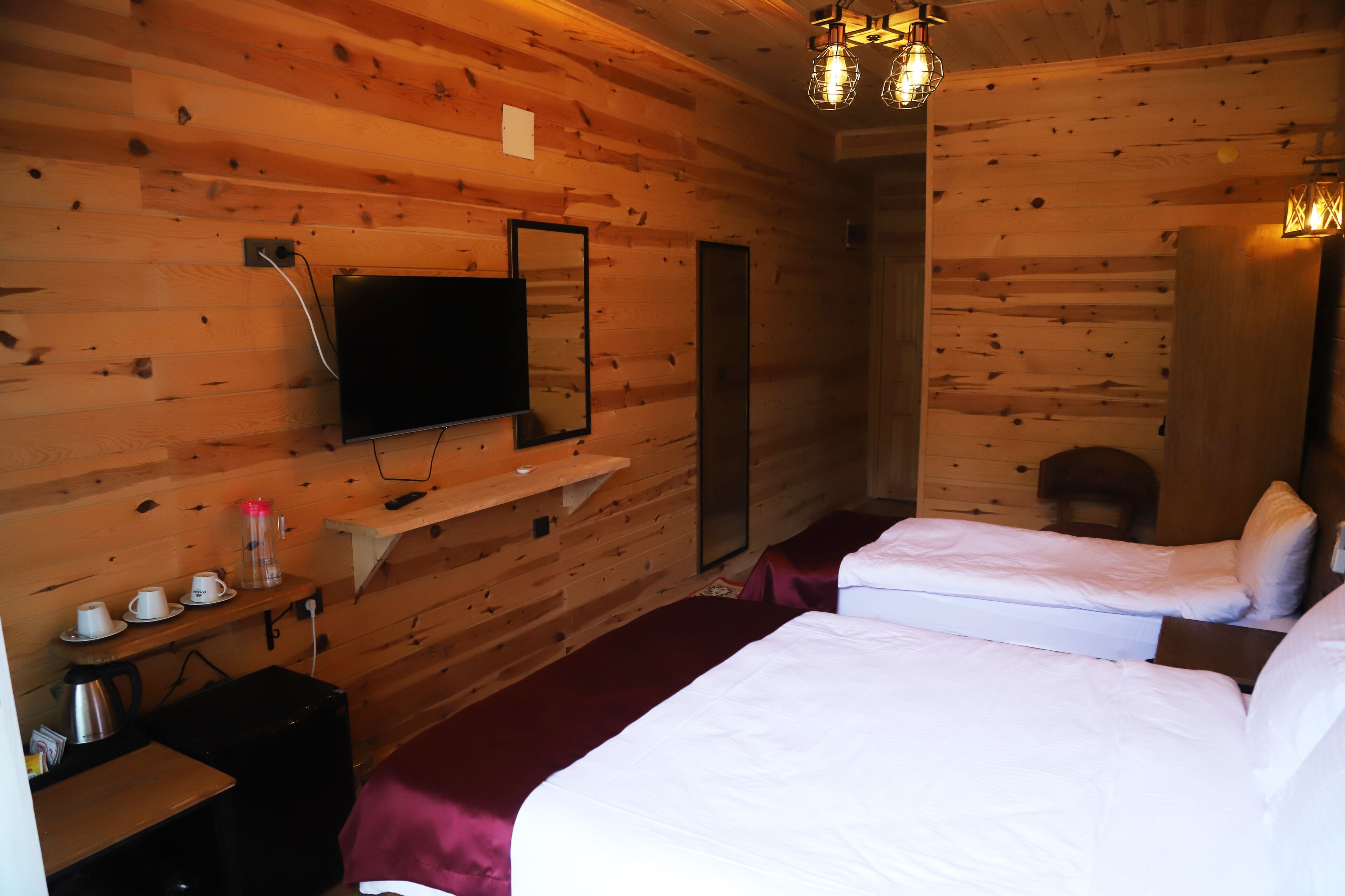 Quarto estilo cabana de madeira com duas camas, televisão e pequena cozinha.