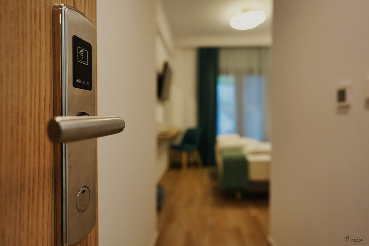 Quarto de hotel com porta de madeira, uma cama, uma escrivaninha e uma cadeira.