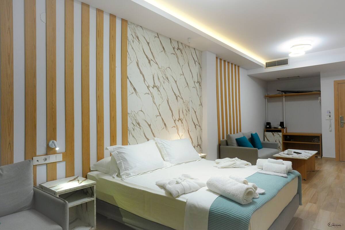 Quarto de hotel moderno com cama, mesas de cabeceira, um sofá e um closet espaçoso.