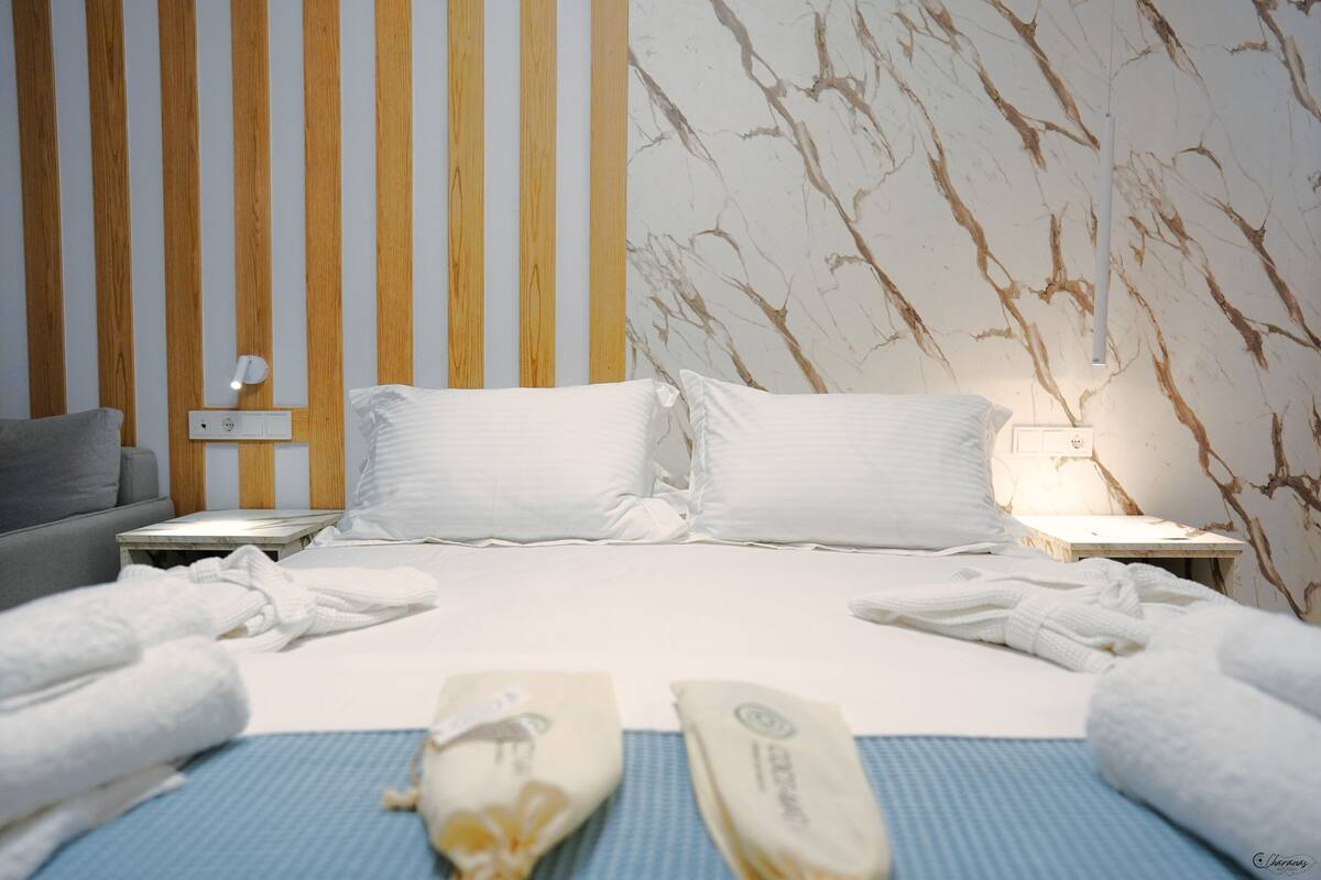Quarto de hotel com cama, duas almofadas, mesa de cabeceira, luminária e toalhas.