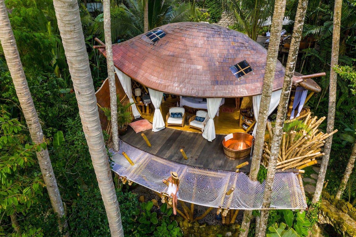 Uma casa na árvore com telhado de palha, deck de madeira e área de estar.