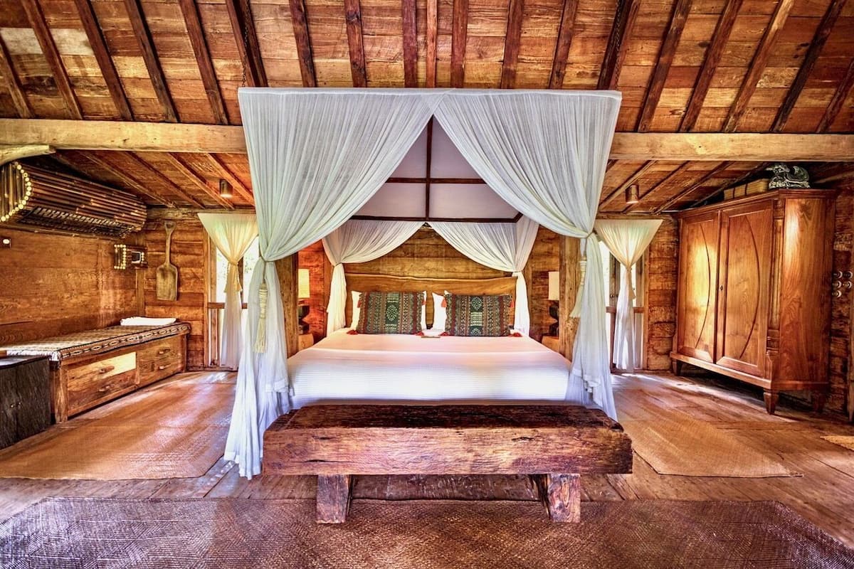 Quarto rústico de madeira com cama de dossel, móveis de madeira e teto alto.