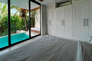 Quarto com uma janela ampla com vista para uma piscina e vegetação exuberante.