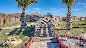 Um calçadão de madeira leva a uma área de praia com palmeiras e uma cerca de madeira.