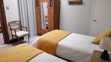 Quarto com duas camas, um guarda-roupa de madeira, uma cadeira e uma mesa de cabeceira com abajur.