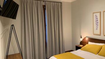 Quarto de hotel com uma cama, uma mesa de cabeceira, televisão fixada na parede e uma janela com cortinas.