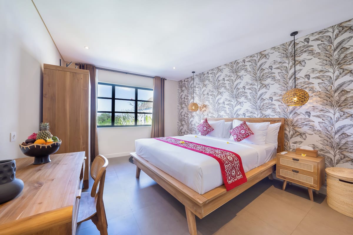 Quarto moderno com cama grande, mobiliário de madeira, uma fruteira e vista para o exterior.