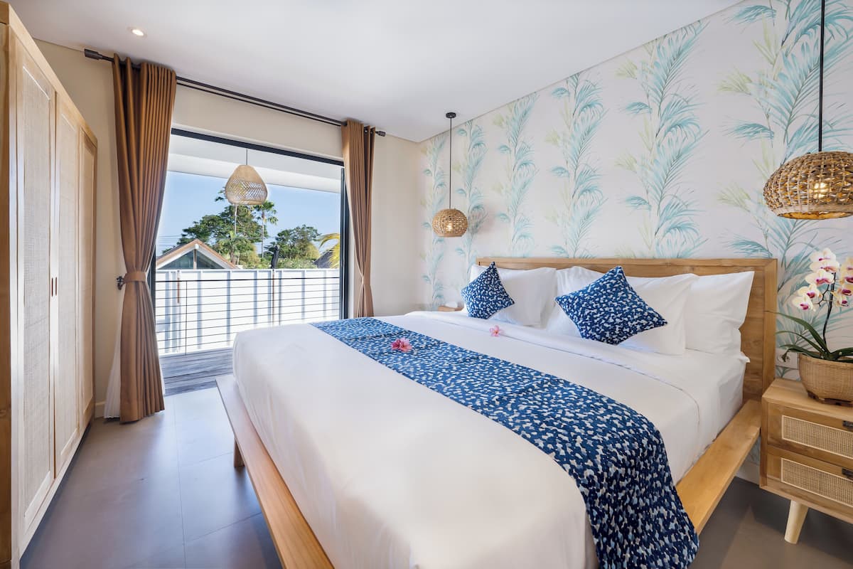 Quarto de hotel moderno com uma cama grande, varanda e vista, e um design de papel de parede com tema tropical.