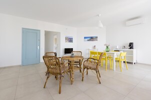 Uma sala de estar moderna com área de jantar, apresentando cadeiras de vime, uma mesa redonda e um sofá branco.