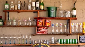 Uma área de bar com prateleiras de garrafas, copos e petiscos. Uma placa diz 'Territorio Guane'.